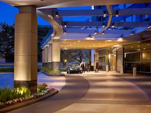 Entrada de hotel com design moderno, uma galeria coberta e um carro estacionado na frente.