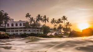 Um hotel na praia com piscina, palmeiras e um pôr do sol.
