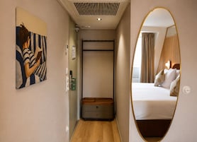 Quarto de hotel com uma cama, mesa de cabeceira, espelho e um quadro na parede.