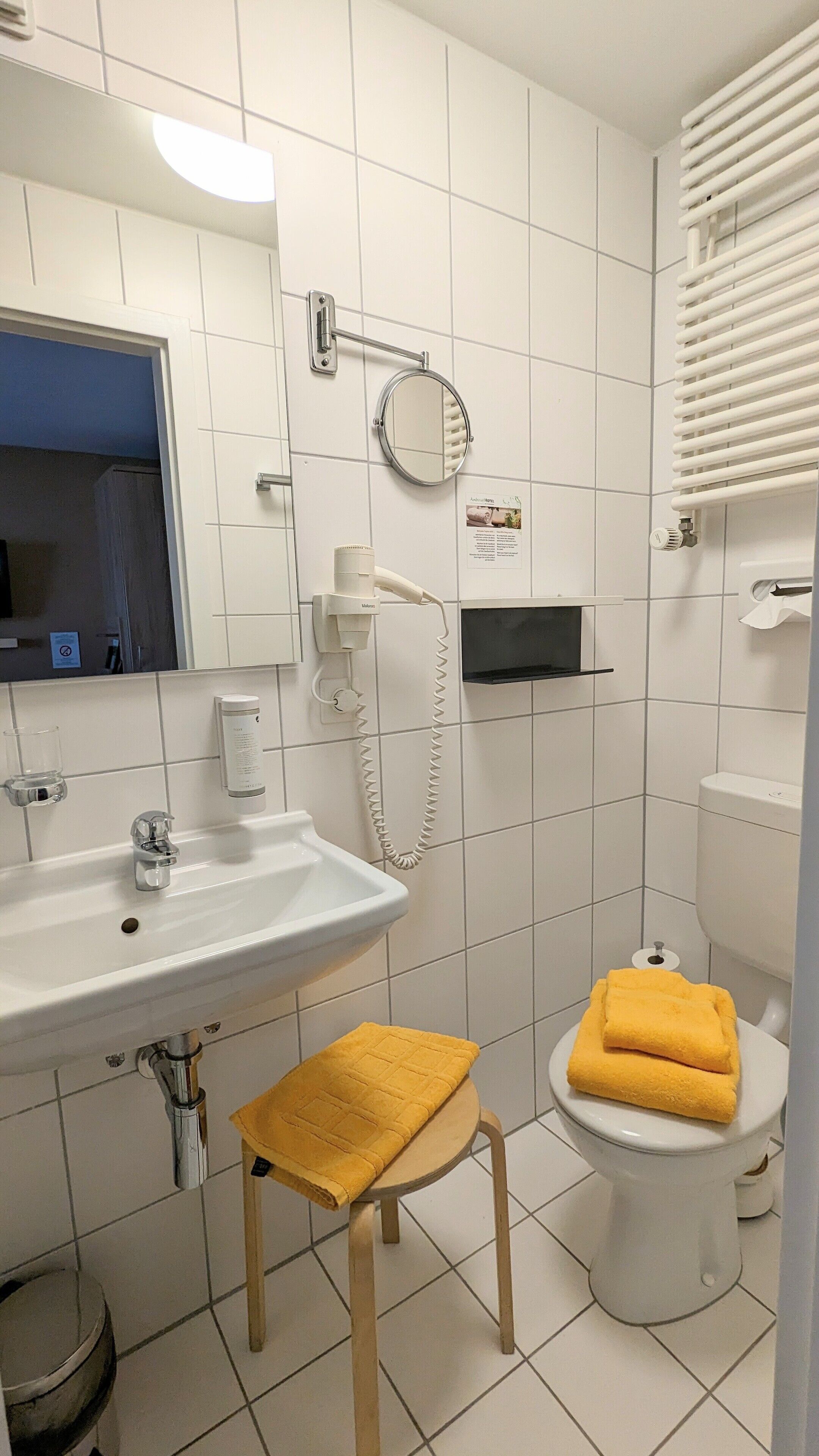Um banheiro com pia, espelho, porta-toalhas, vaso sanitário e um banquinho pequeno.