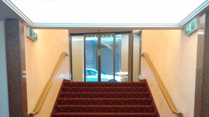 Escada revestida com carpete e corrimãos, que dá acesso a um elevador.