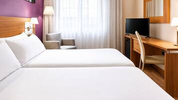 Quarto de hotel com duas camas, uma escrivaninha, televisão, uma cadeira e um abajur.