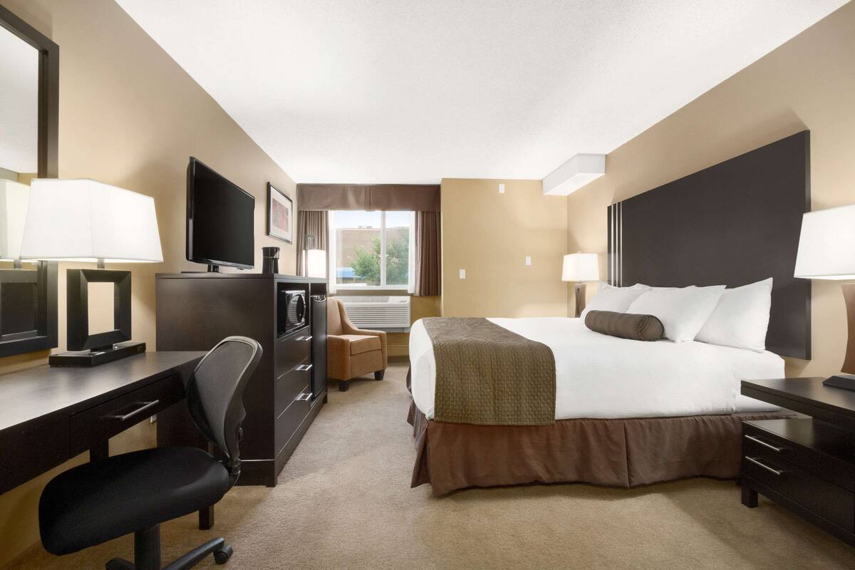 Quarto de hotel com cama, escrivaninha, cadeira, televisão e janela com cortinas.