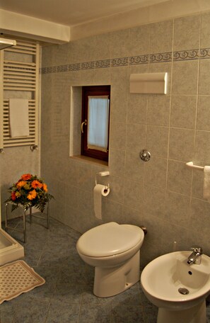 Casa de banho com sanita, bidé, lavatório, para-brisas e janela com cortina.