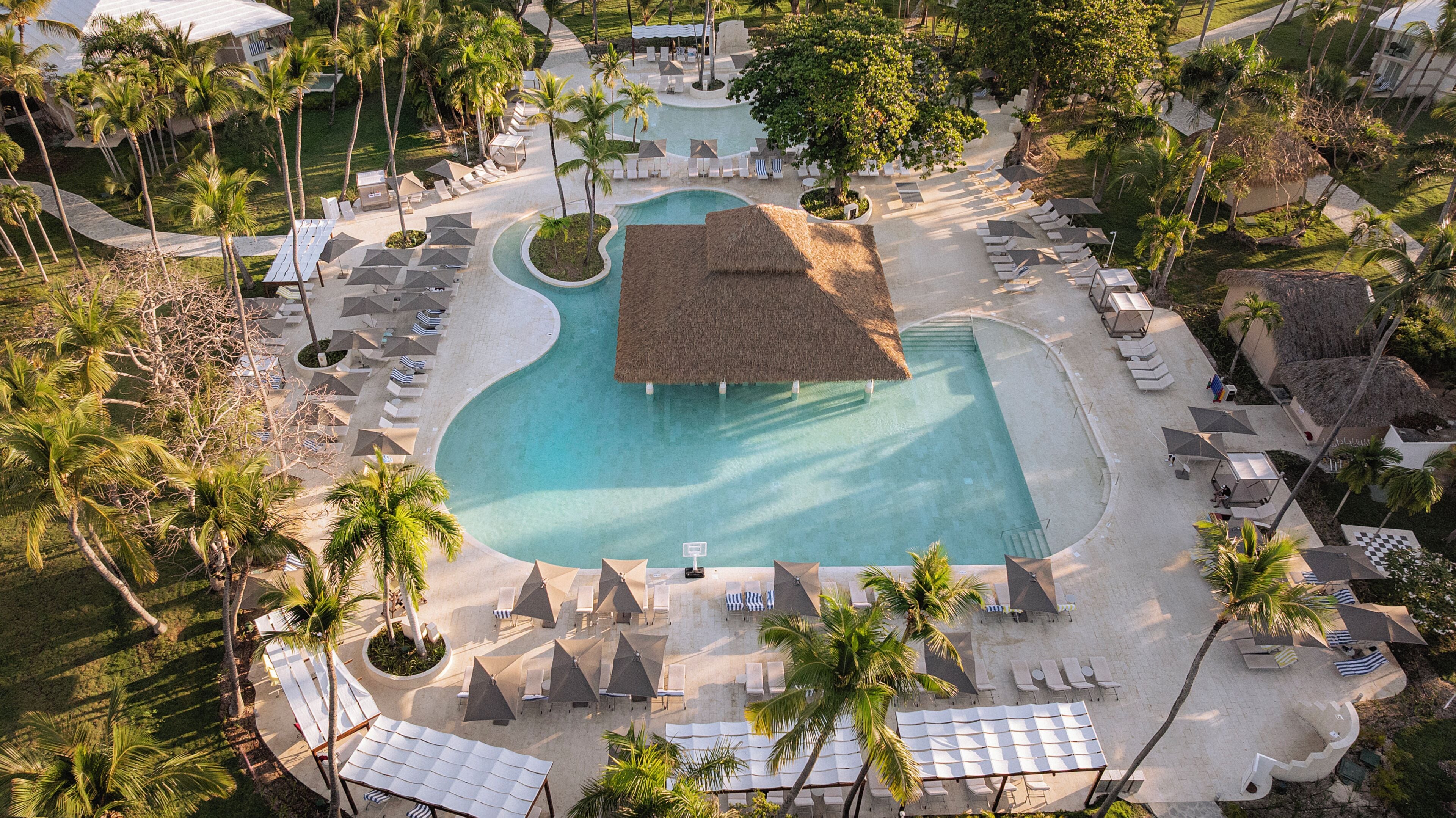 Vista aérea de um resort com piscina central, espreguiçadeiras e palmeiras.