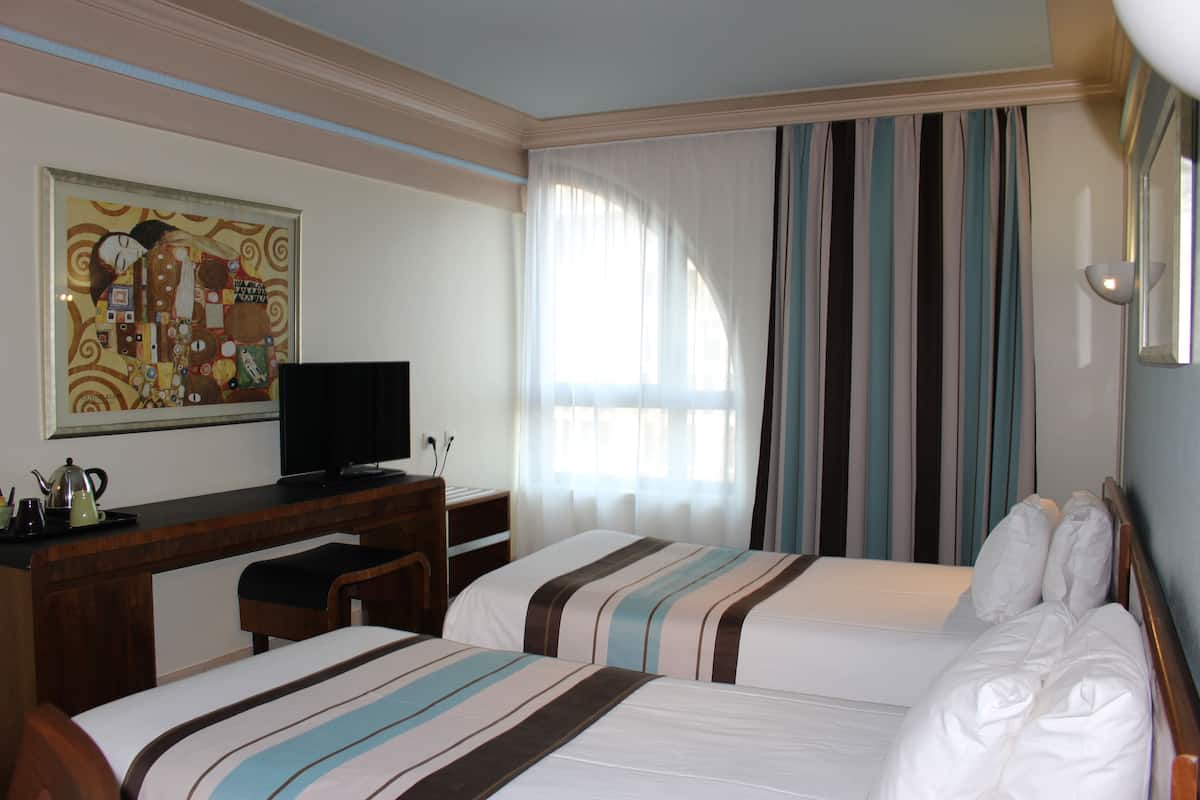 Quarto de hotel com duas camas, uma escrivaninha, televisão e um quadro na parede.