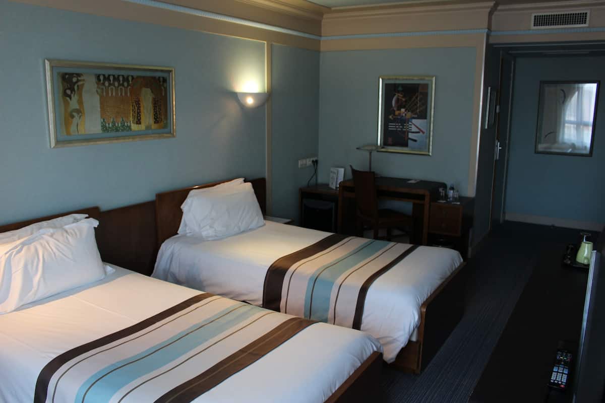 Quarto de hotel com duas camas, uma escrivaninha, uma cadeira e uma televisão.