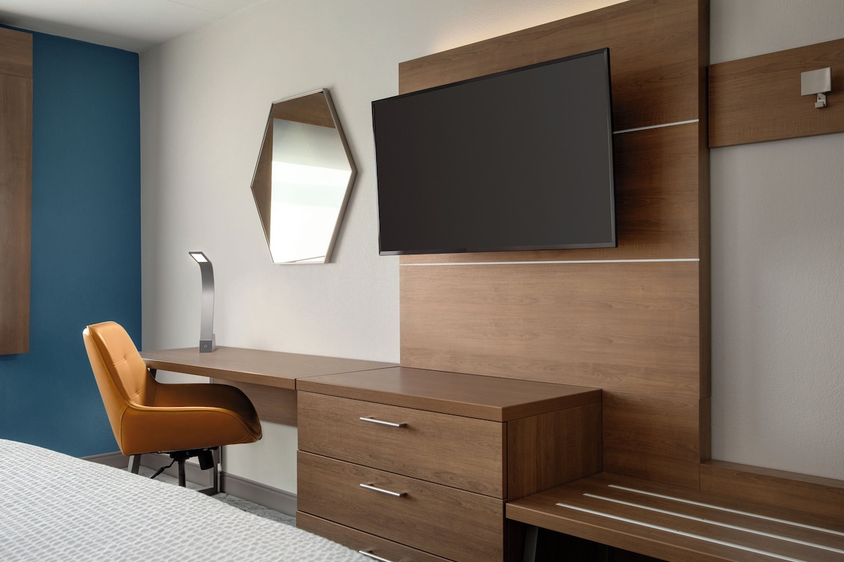 Quarto moderno com uma escrivaninha de madeira, uma cadeira, uma televisão de tela plana e um espelho.