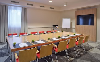 Uma sala de conferências com uma mesa comprida, cadeiras, uma tela de projetor e um quadro branco.