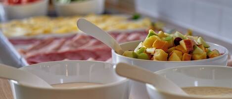 Uma mesa com tigelas de comida, incluindo uma salada de frutas e um prato cremoso, com colheres dentro.