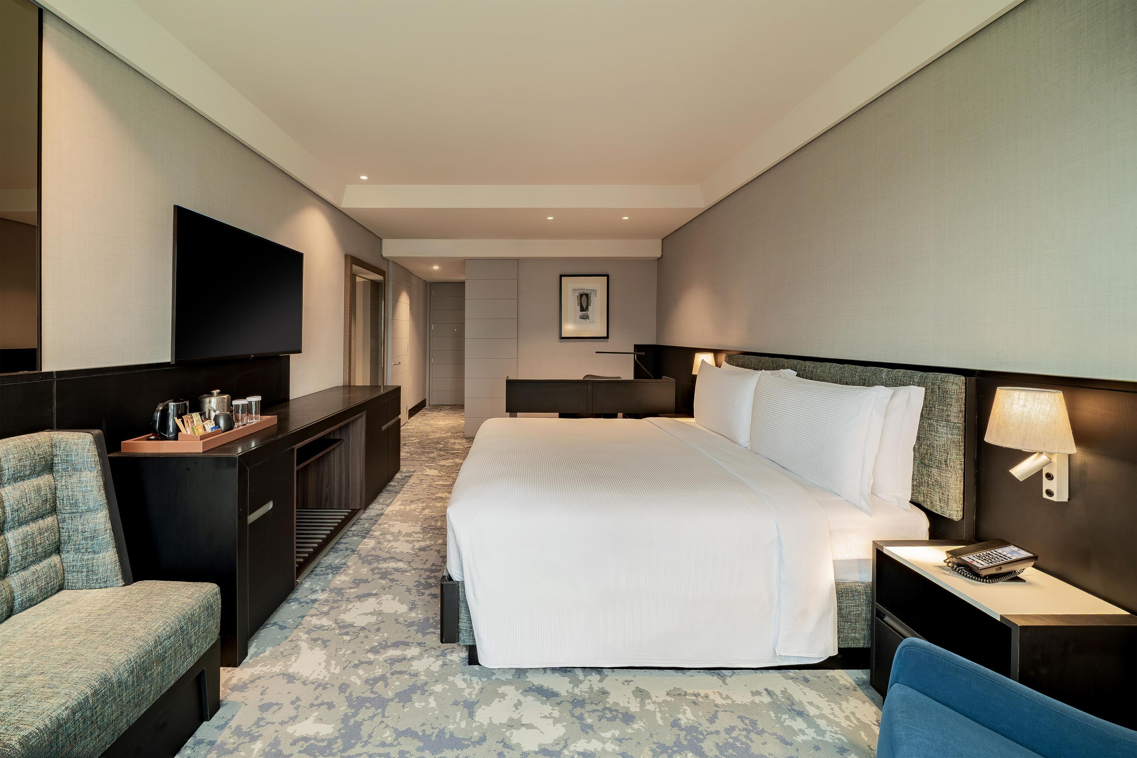 Quarto de hotel com cama, escrivaninha, cadeira, televisão e banheiro.