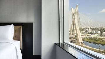 Quarto de hotel com cama e janela com vista para uma ponte moderna e paisagem urbana.