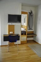 Quarto compacto com escrivaninha, cadeira, cama e televisão.