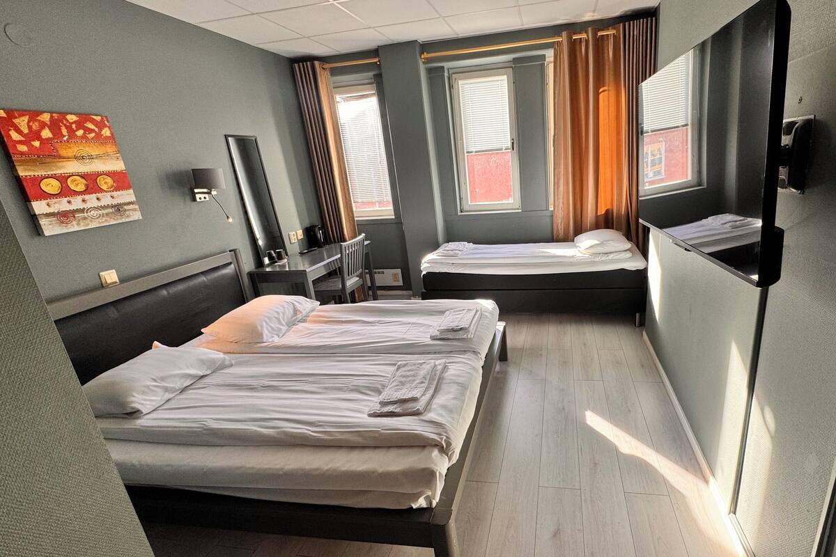 Quarto de hotel com duas camas, uma escrivaninha, uma cadeira e uma janela com cortinas.