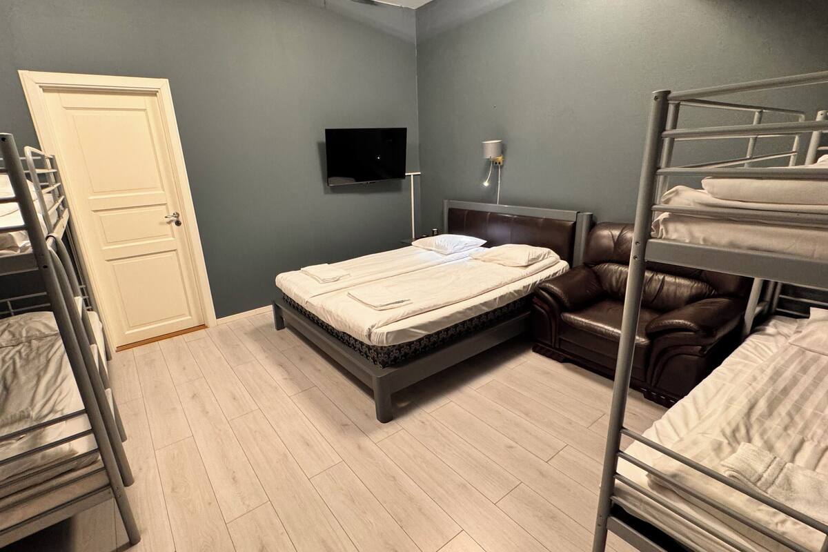 Quarto com beliches, uma cama de solteiro, uma TV e uma porta.