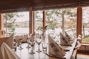 Mesa posta com taças de vinho e talheres, com vista para um lago deslumbrante.