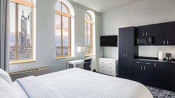Quarto de hotel com cama grande, escrivaninha, cadeira, televisão e cozinha compacta.