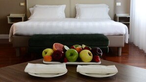 Uma cama bem arrumada com lençóis brancos, um cobertor verde e um prato de frutas na mesinha de cabeceira.
