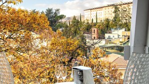 Varanda com mesa e cadeiras, vista para paisagem urbana com folhagem de outono e edifícios.