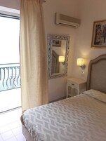 Quarto de hotel com cama, mesa de cabeceira, espelho e ar condicionado fixado na parede.