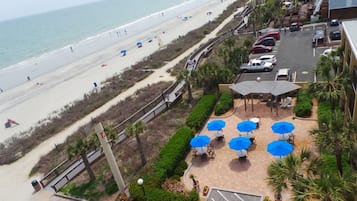 Um hotel à beira-mar com área de pátio, guarda-sóis e assentos, estacionamento e vista para a praia.