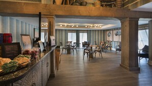 Um restaurante com balcão exibindo doces e um cardápio, piso de madeira e teto alto com detalhes decorativos.