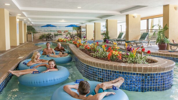 Uma piscina interior com toboáguas azuis, espreguiçadeiras e plantas em vasos.