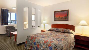 Quarto de hotel com uma cama grande, duas mesas de cabeceira com luminárias, uma cadeira, uma escrivaninha e uma janela com cortinas.