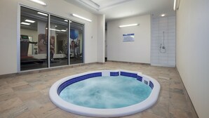 Piscina interna com borda em azulejo, rodeada por piso e paredes também revestidas em azulejo, e uma porta de vidro que dá para outro espaço com equipamentos de ginástica.