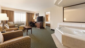 Quarto de hotel com sofá, escrivaninha, televisão, banheiro com banheira e um espelho grande.