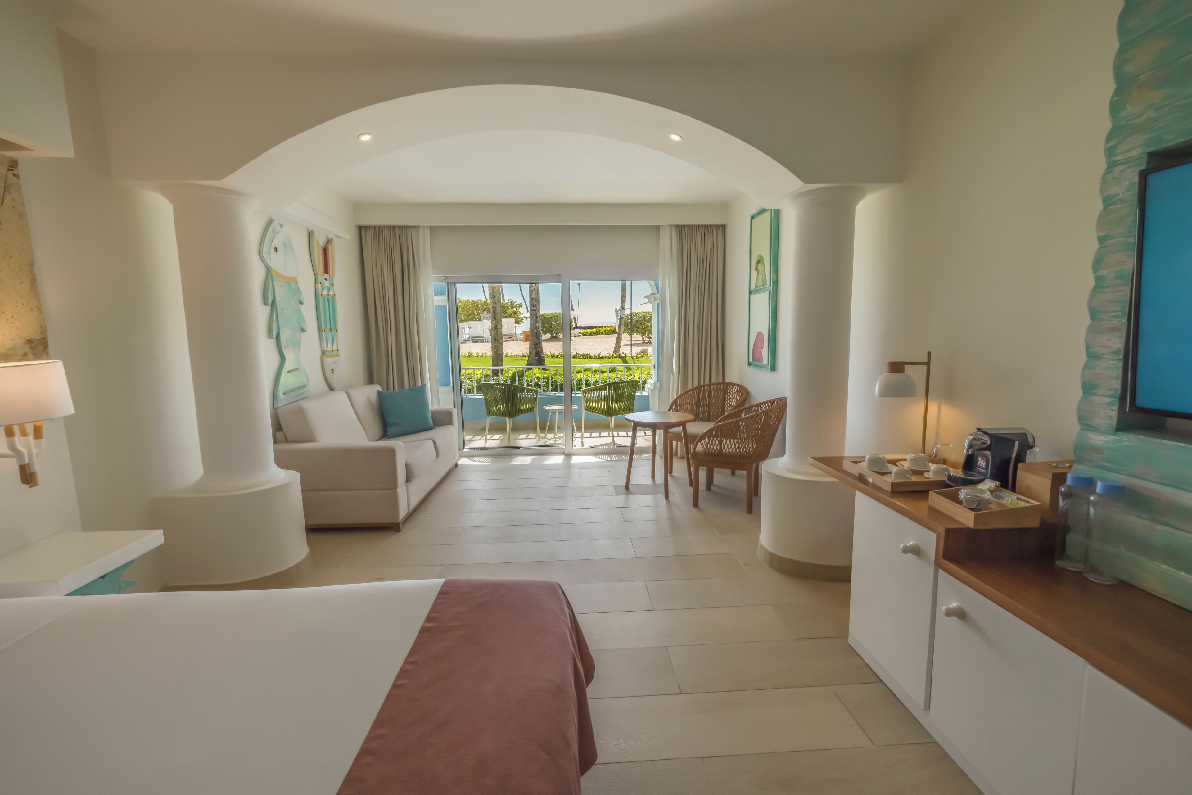 Quarto de hotel com cama, sofá, mesa de jantar e varanda com vista.