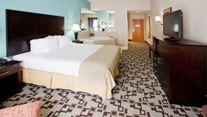 Quarto de hotel com uma cama grande, uma escrivaninha com telefone, uma televisão em um armário de madeira e banheiro com banheira e espelho.