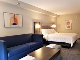 Quarto de hotel com cama, sofá, mesa pequena e duas luminárias fixadas na parede.