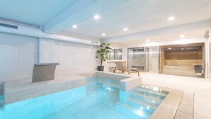 Piscina interior moderna com água cristalina, área de estar com uma planta e sauna.