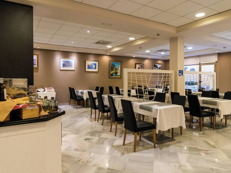 Um restaurante com chão de mármore, mesas com toalhas brancas, cadeiras pretas e quadros nas paredes.