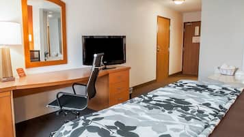 Quarto de hotel com uma cama, escrivaninha com cadeira, televisão, espelho e porta.