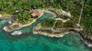 Vista aérea de um resort à beira-mar com praia, águas turquesa cristalinas e vegetação exuberante.