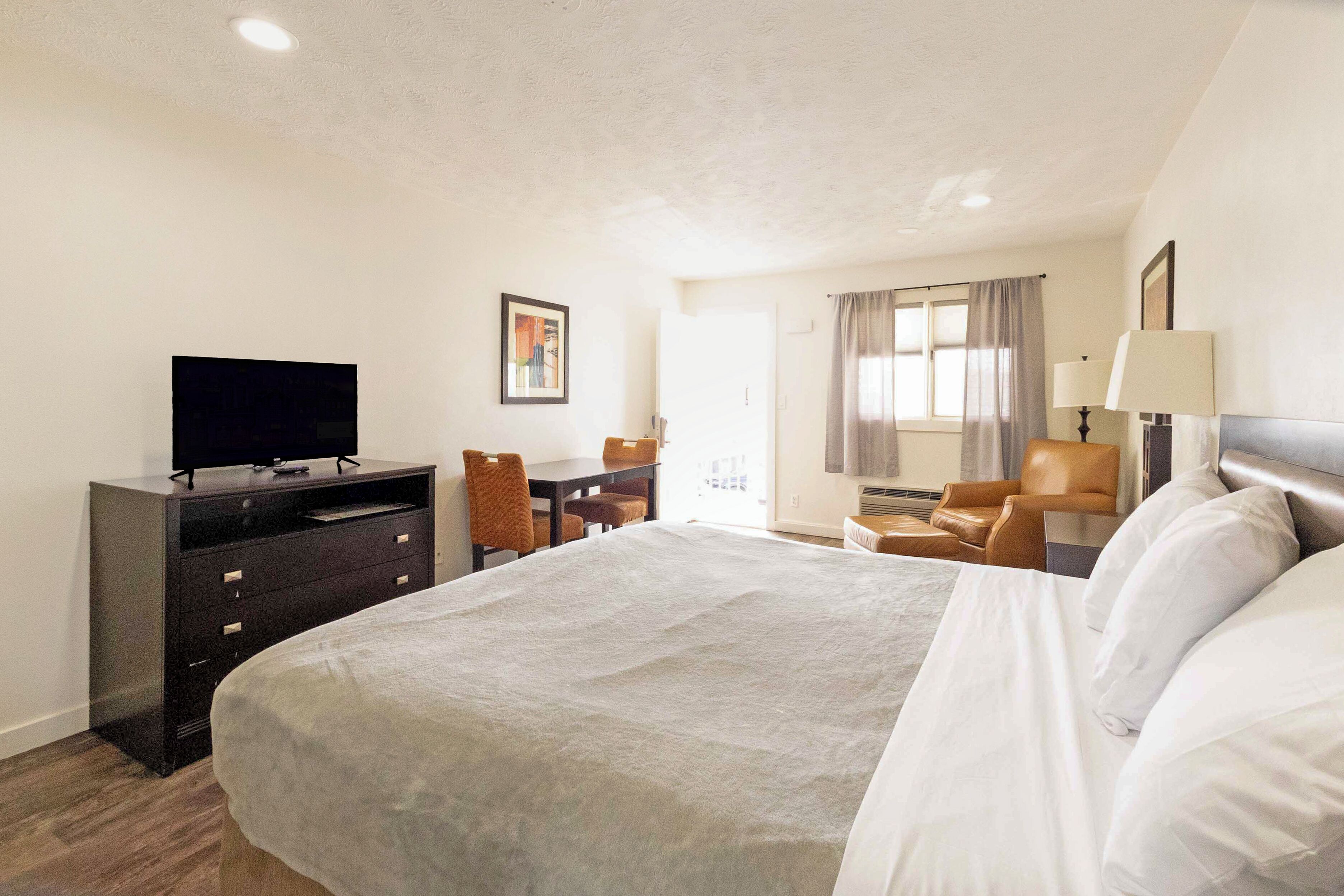 Quarto de hotel com cama, escrivaninha, televisão, poltrona e janela com cortinas.
