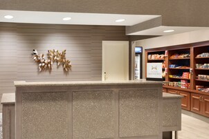 Uma área de recepção de hotel com design moderno, destacando um balcão com superfície texturizada e uma obra de arte decorativa na parede.
