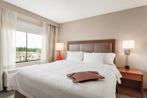 Quarto de hotel com uma cama grande, duas luminárias de cabeceira, uma mesa de cabeceira e uma janela com cortinas.