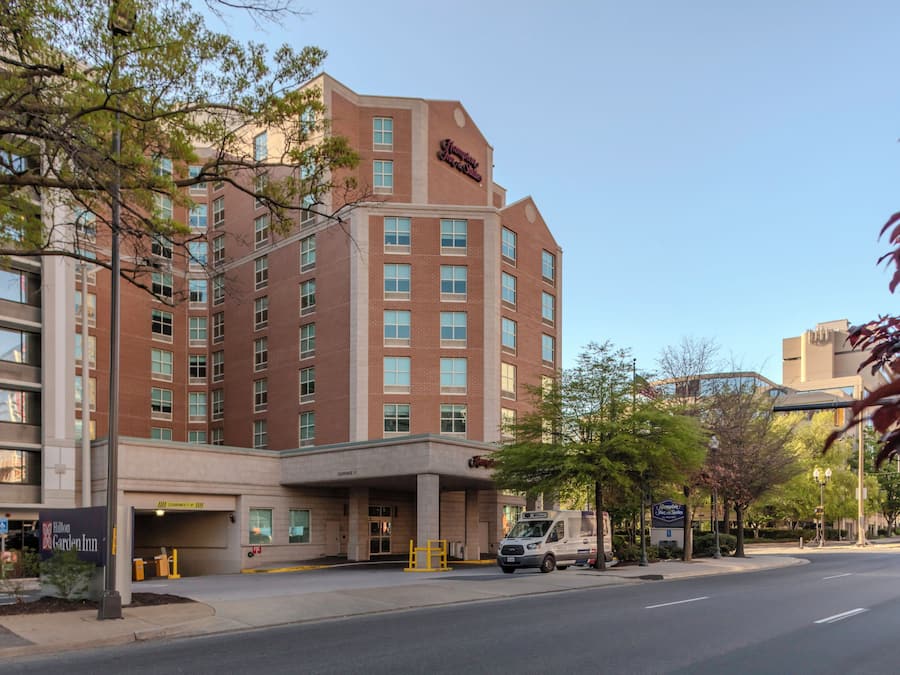 Um hotel de vários andares com fachada de tijolos, entrada central e área de estacionamento.