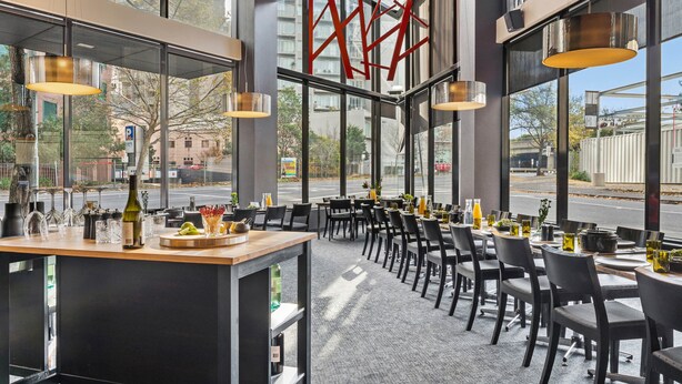 Restaurante moderno com amplas janelas, área de bar e cadeiras pretas.