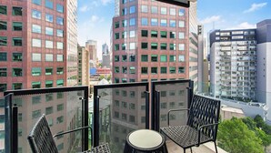 Uma varanda com duas cadeiras e uma mesa, com vista para um horizonte urbano com edifícios altos.