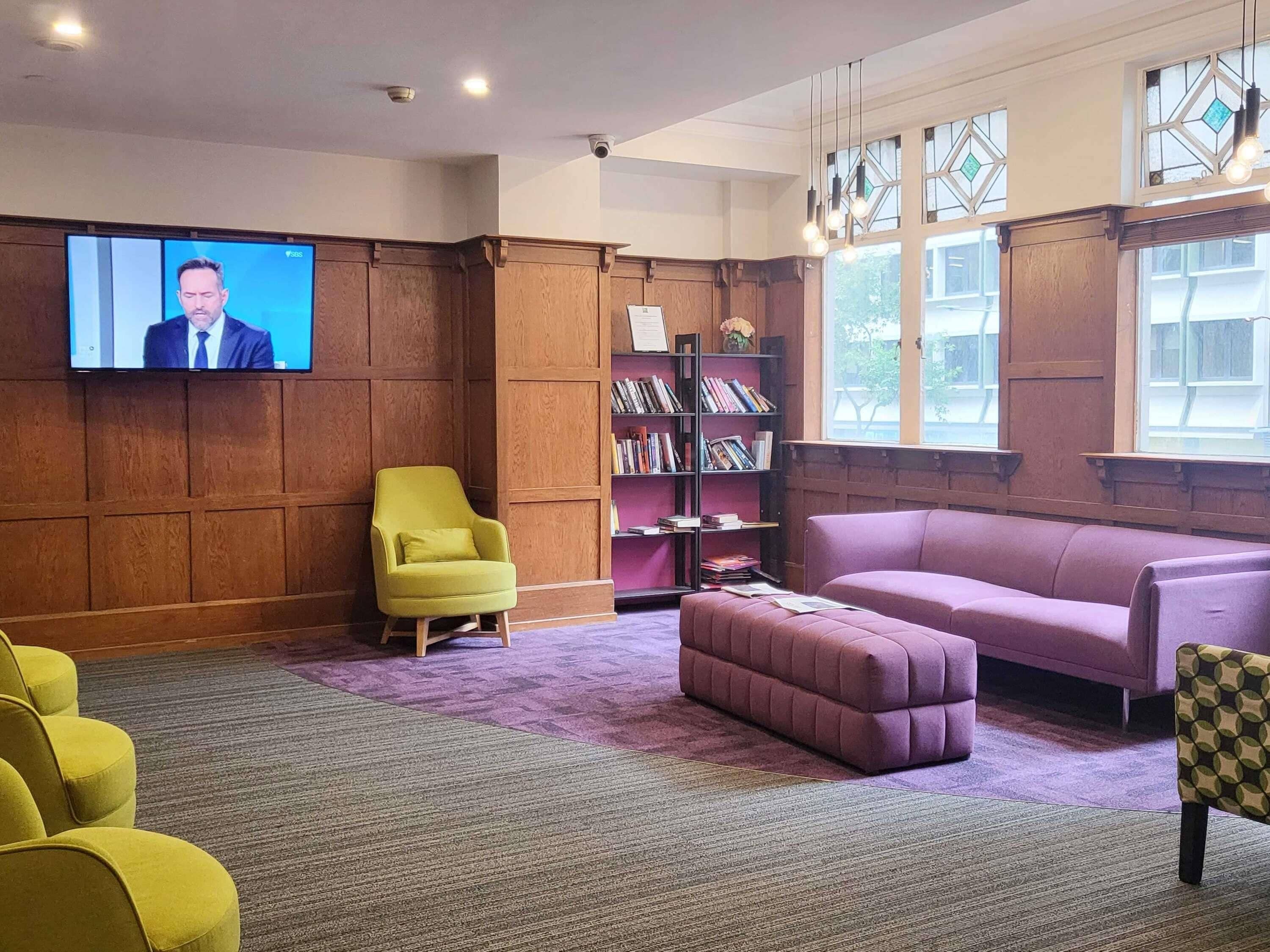 Quarto com televisão, estantes, sofá roxo e poltrona amarela.