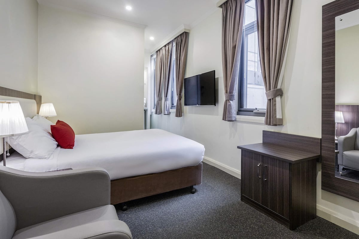 Quarto de hotel com cama, abajures, televisão, secretária e uma cadeira.