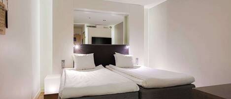 Quarto de hotel moderno com uma cama grande, uma mesinha de cabeceira e um espelho sobre a cama.