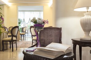 Um quarto bem iluminado com área de jantar, uma cadeira de vime, uma mesa com um livro e um copo, e um abajur.