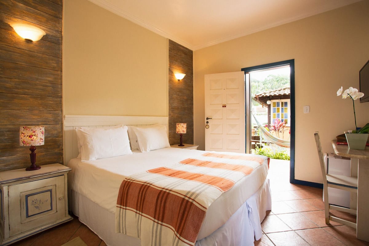 Um quarto com cama, abajures, porta que dá para o exterior e vista para o exterior.