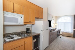 Cozinha compacta de hotel com armários de madeira, micro-ondas, geladeira, cafeteira e pia.