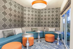 Uma área de estar moderna com um sofá azul, pufes laranja e papel de parede estampado.